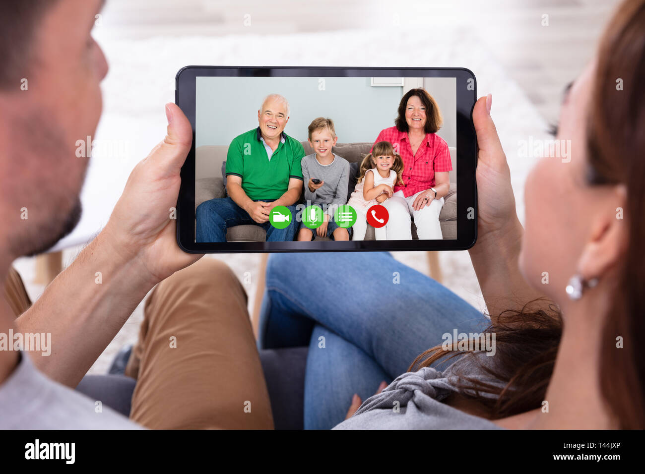Couple Sitting On Sofa Video Conferencing With Their Happy Family Using ...