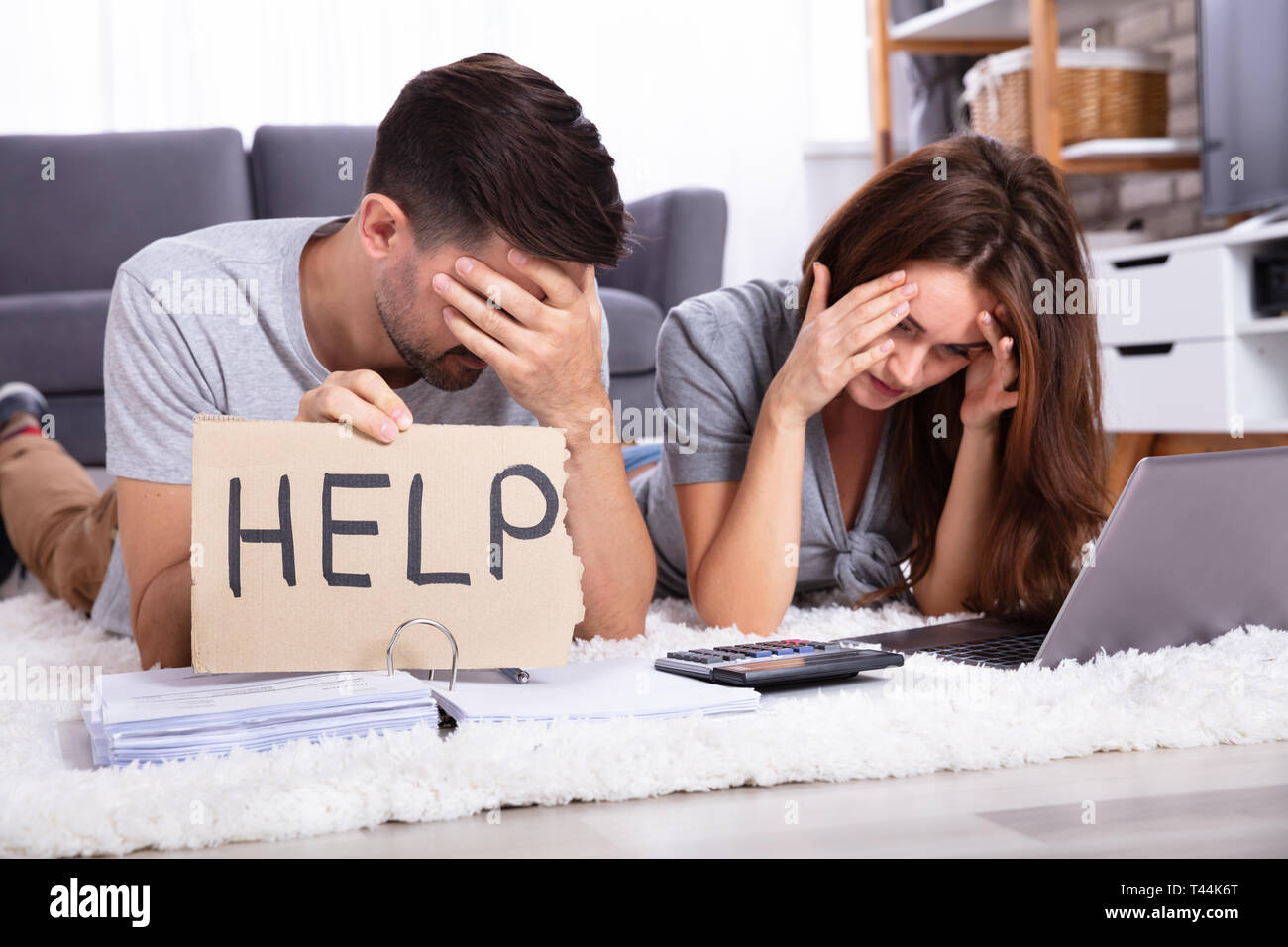 Sad Young Couple Lying On Carpet Holding Help Sign While Calculating ...