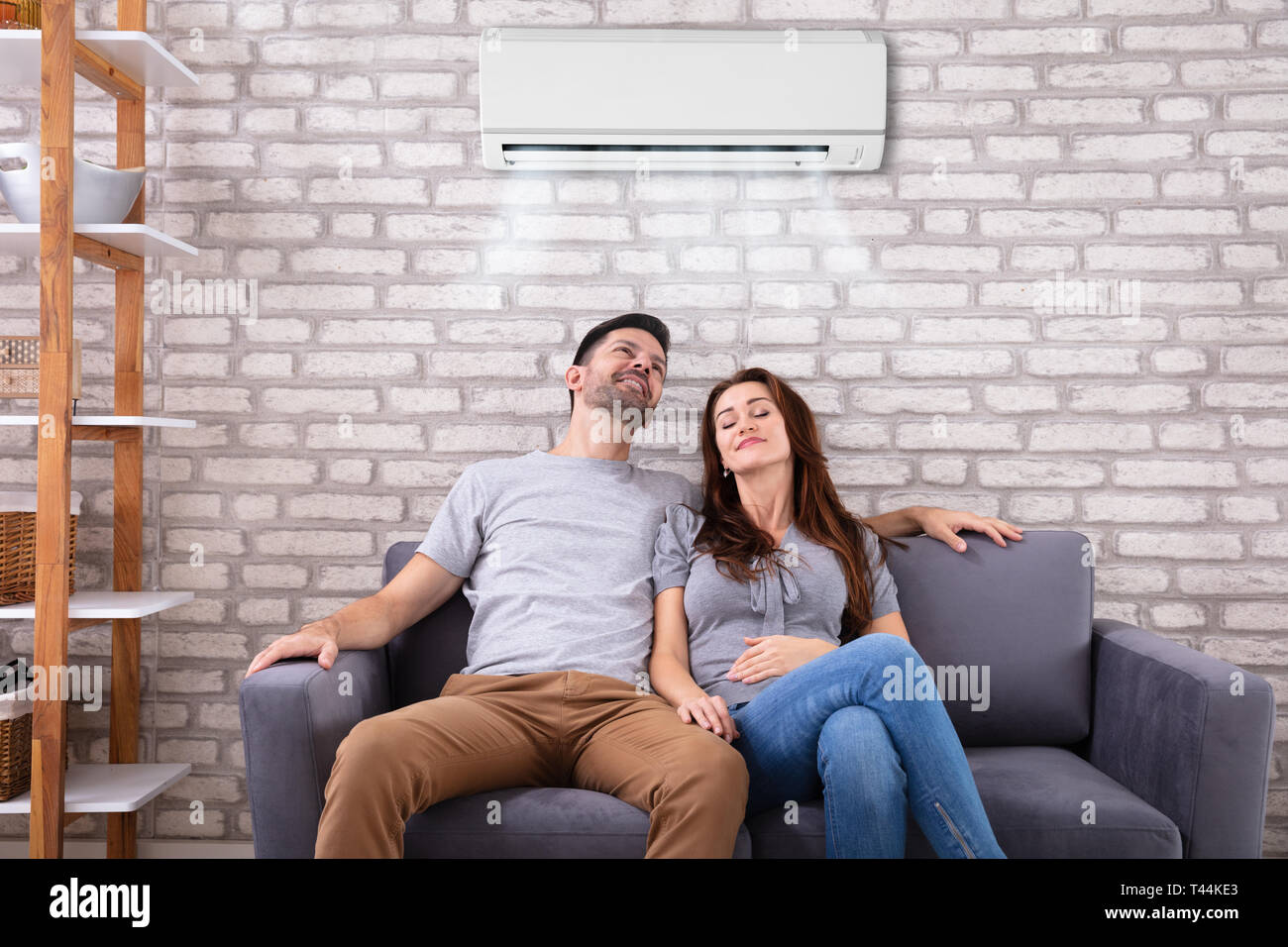 Happy Young Couple Sitting Under Air Conditioner On Couch At Home Stock ...