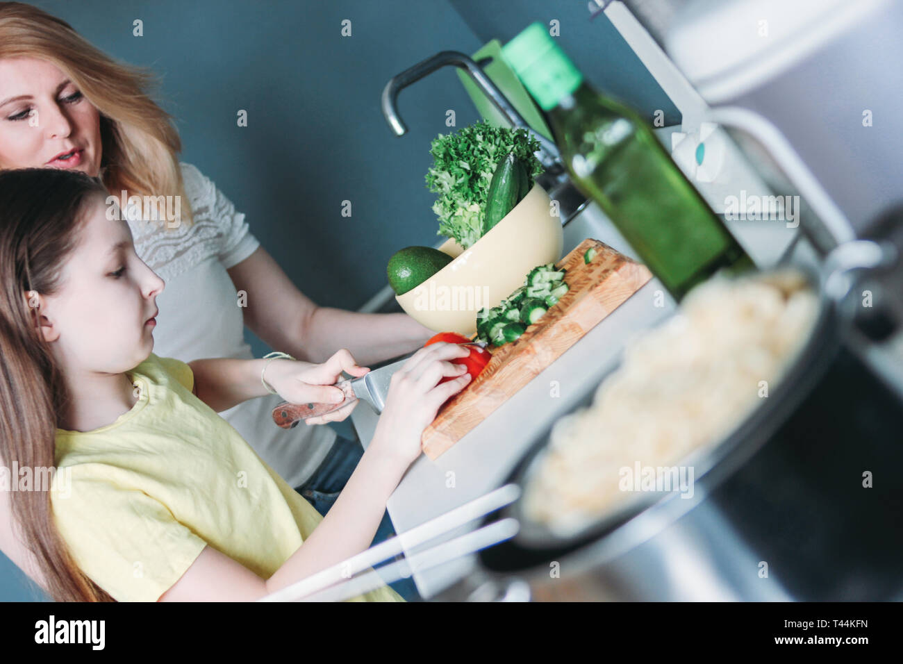 Tween girl and her mother making vegetable salad in the kitchen at home ...