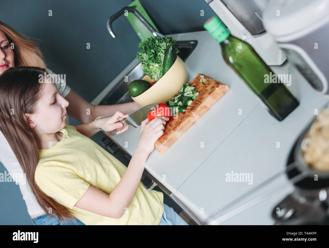 Tween girl and her mother making vegetable salad in the kitchen at home ...