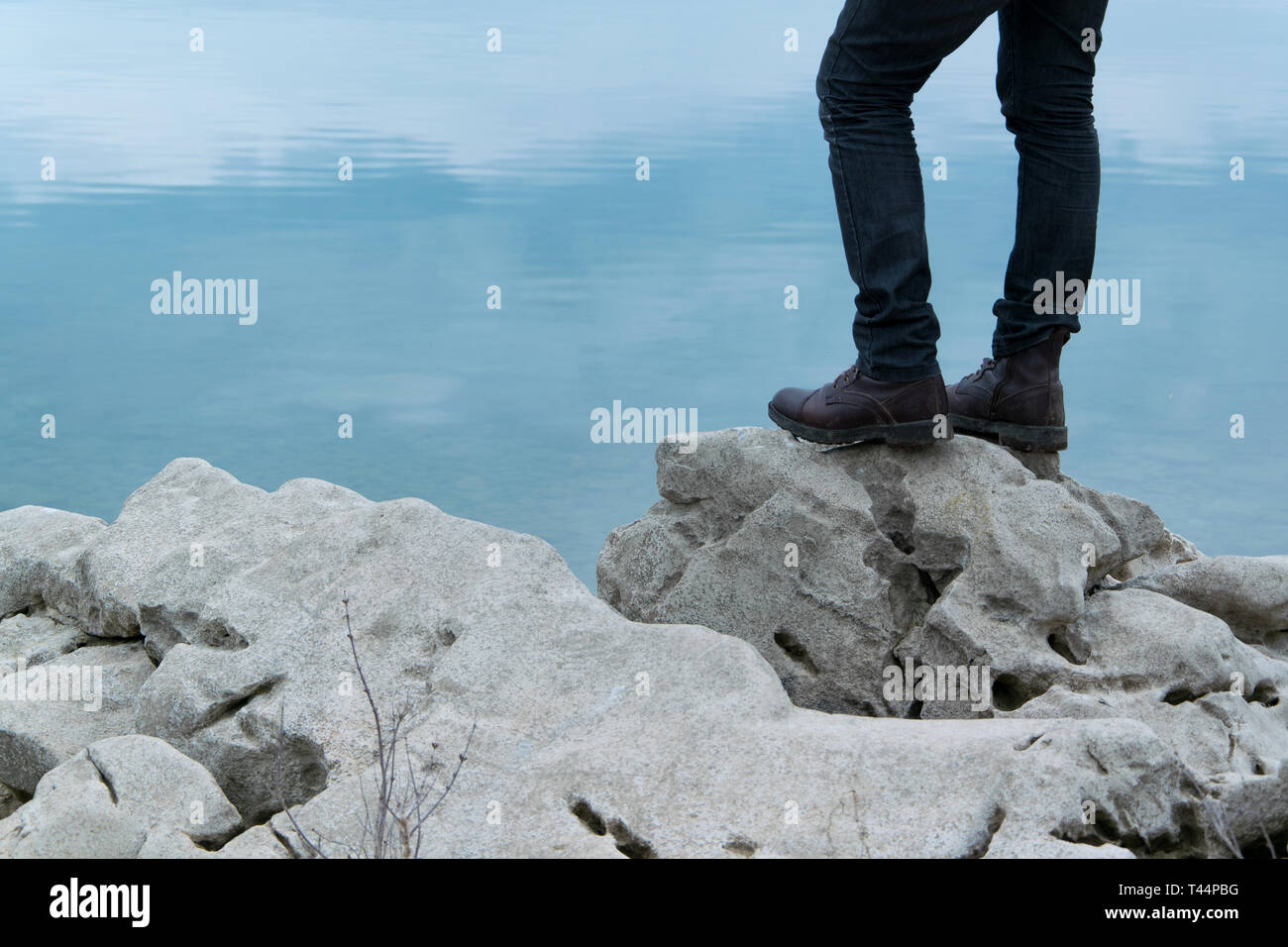 Low angle view of man standing on the rocky cliff, water background ...