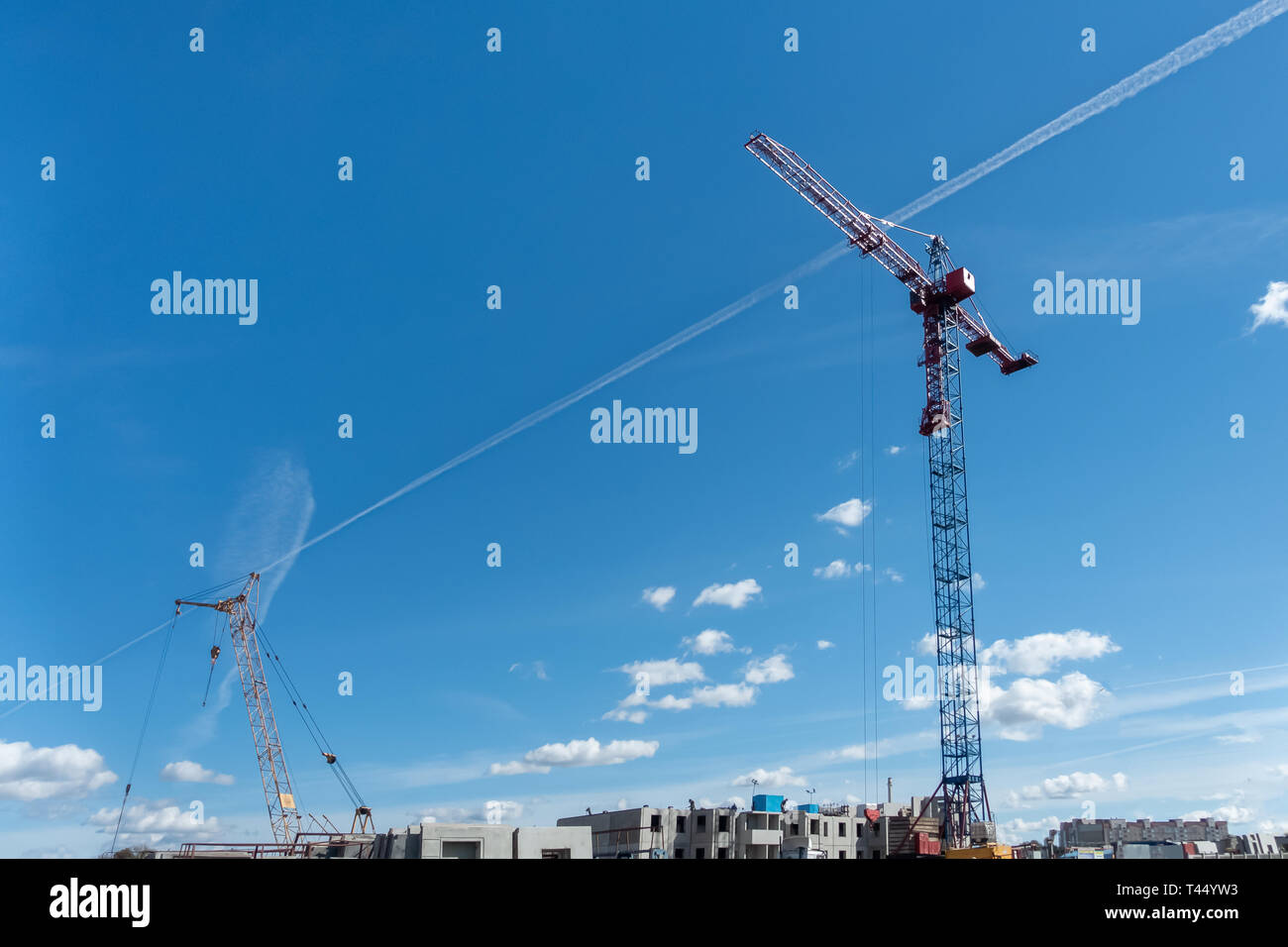 Two tall construction cranes on blue sky background. workers build ...
