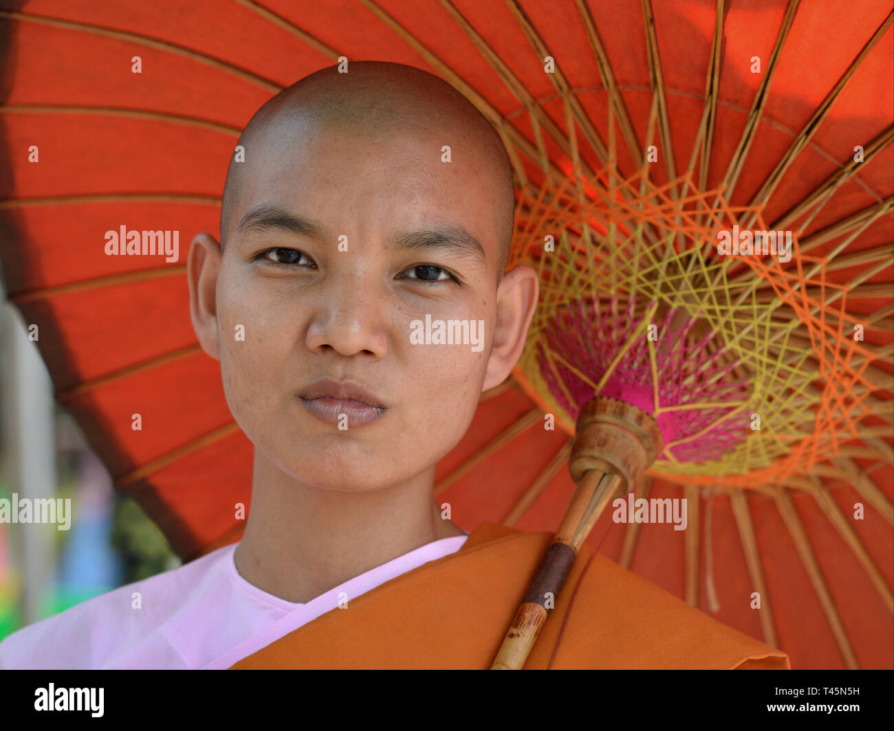 Young Burmese Buddhist nun poses for the camera under a red ...