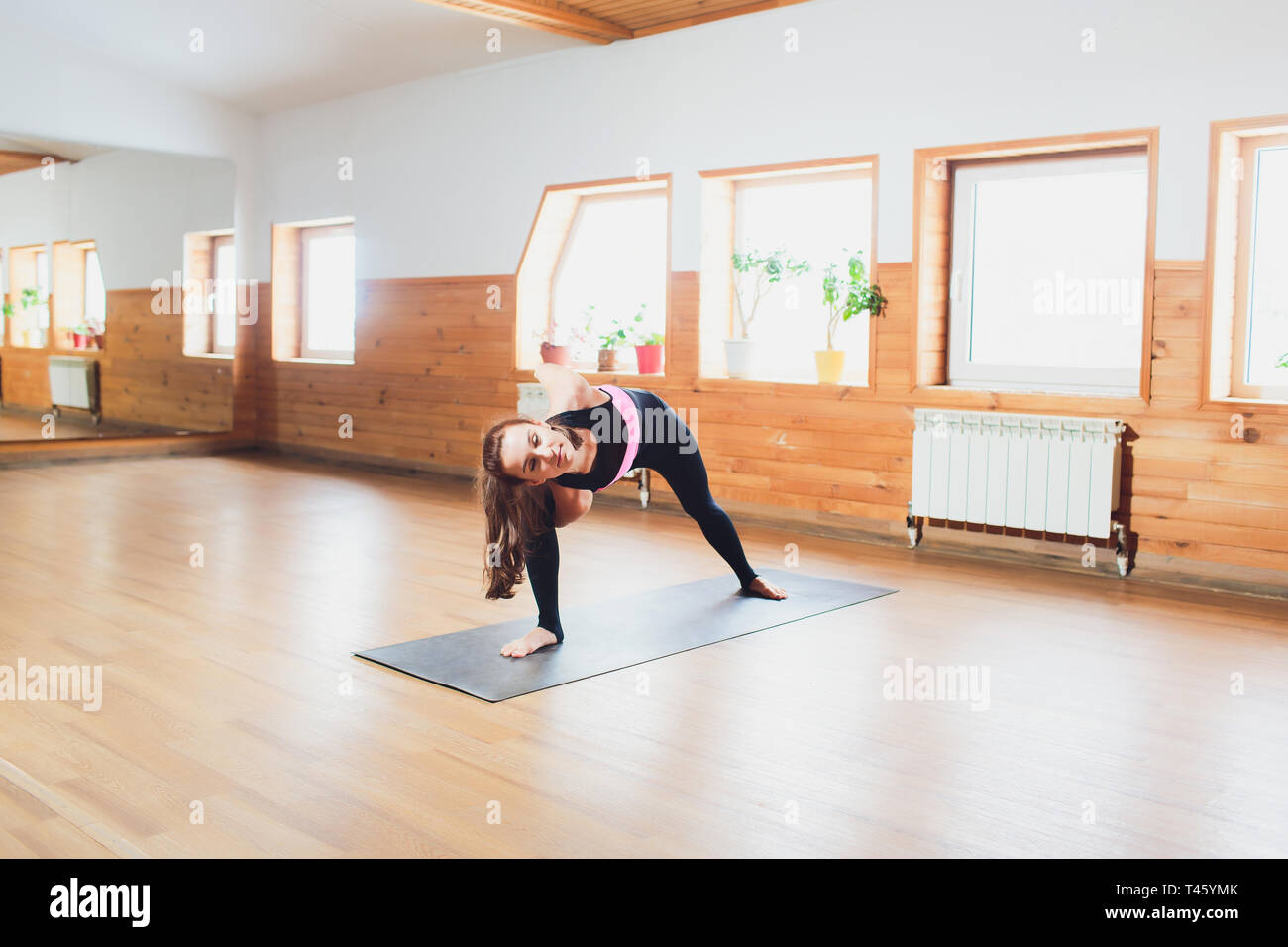 Rear view of young female yogi in sports bra and leggings doing bound ...
