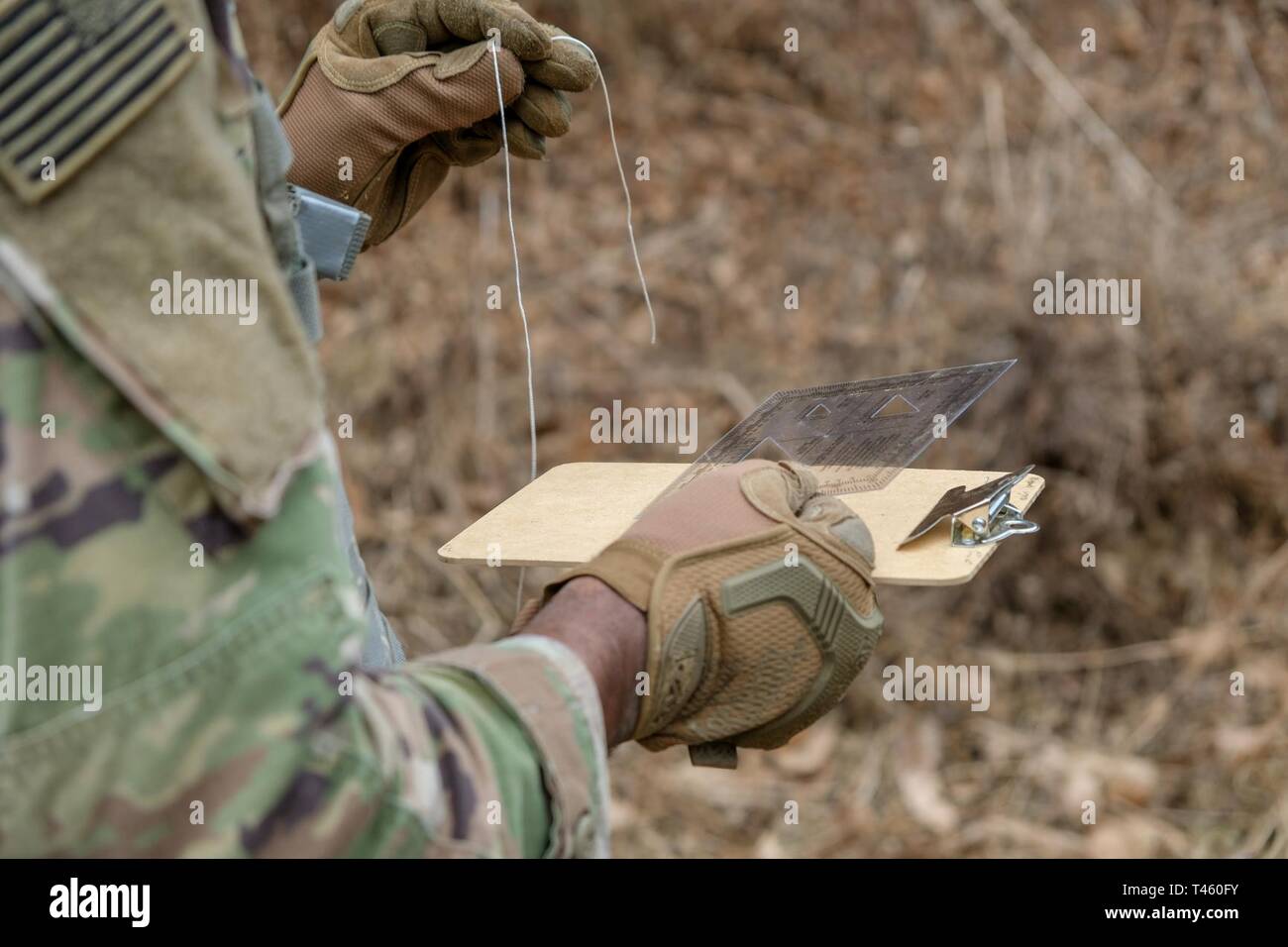 A Soldier prepares his protractor by lacing white string through it to ...