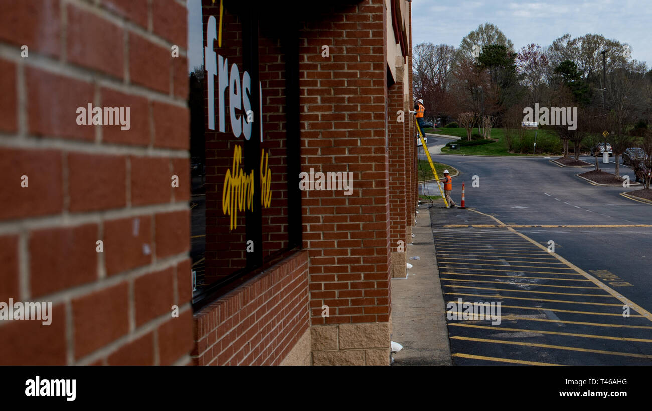 Man on ladder leaning against commercial building wall while another ...