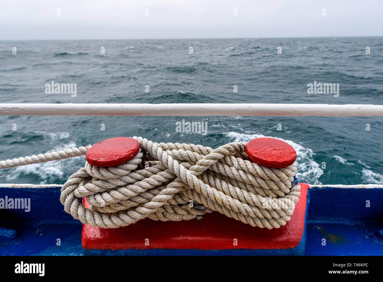 Close up of red double bollard with rope tied around it, ship detail ...