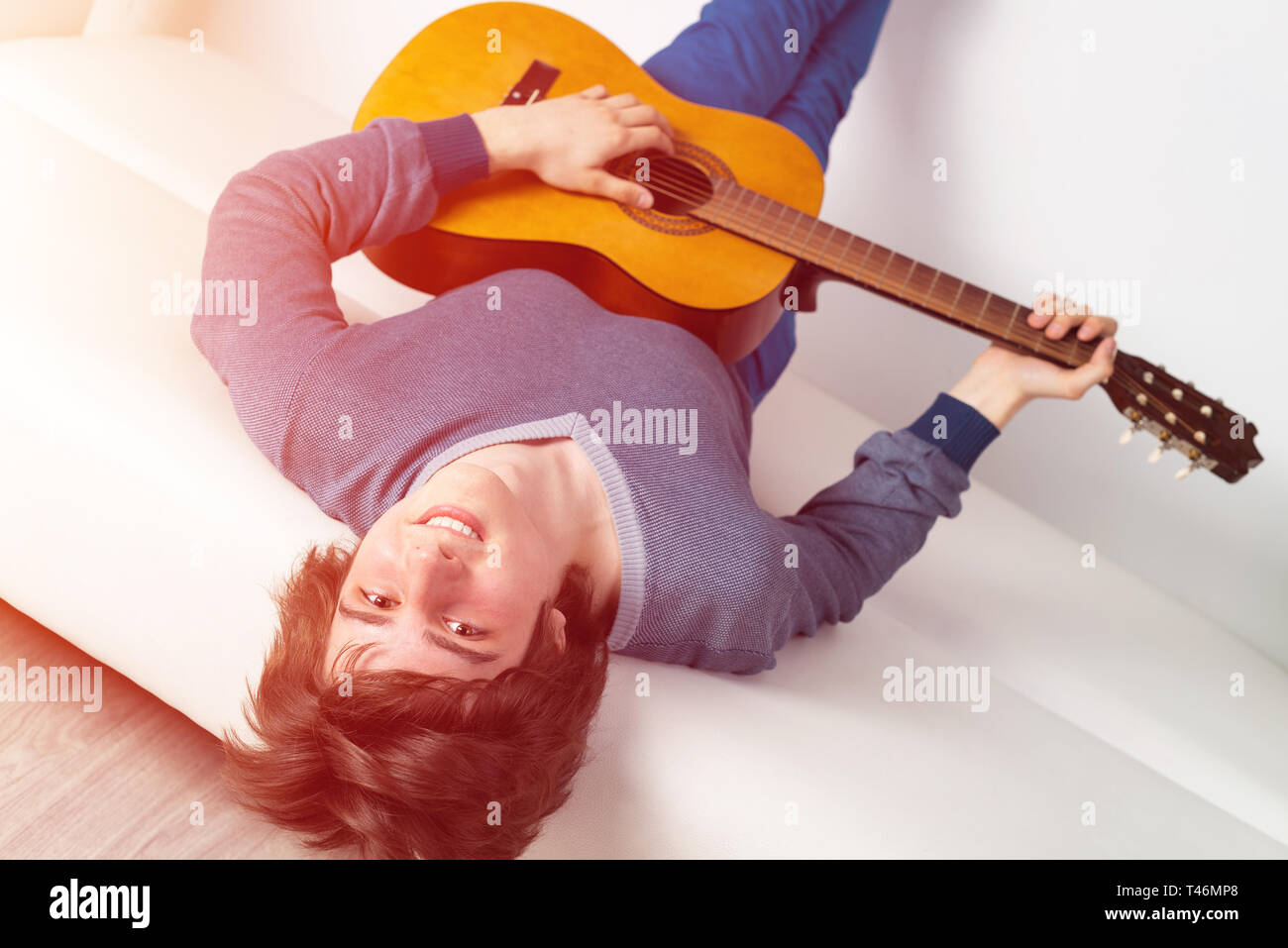 Happy young man lying back on sofa with guitar. Smiling guitarist ...