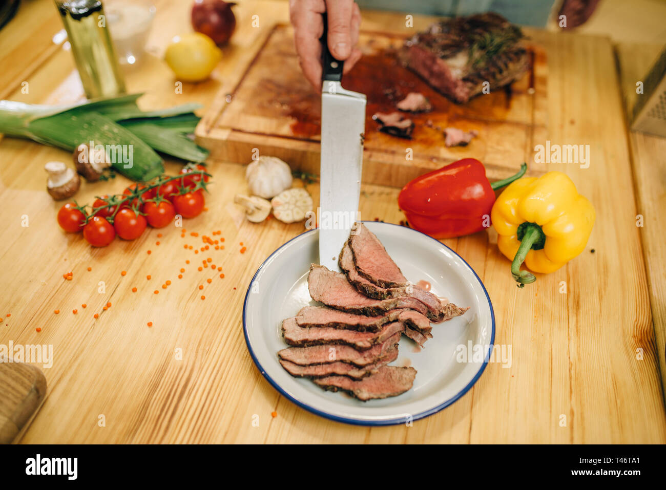 Chef with knife puts roasted meat into the plate Stock Photo - Alamy
