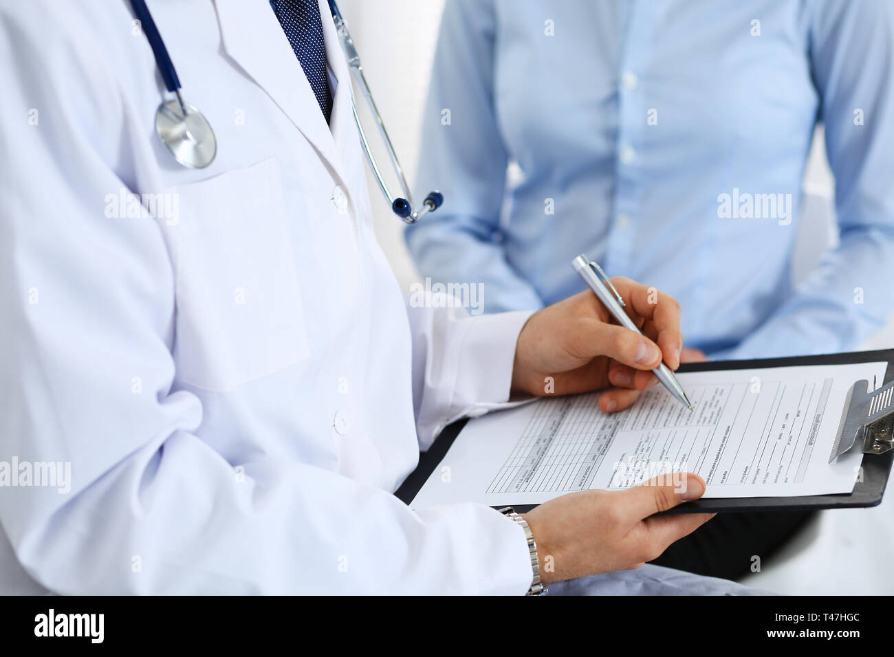 Male doctor holding application form while consulting female patient in ...
