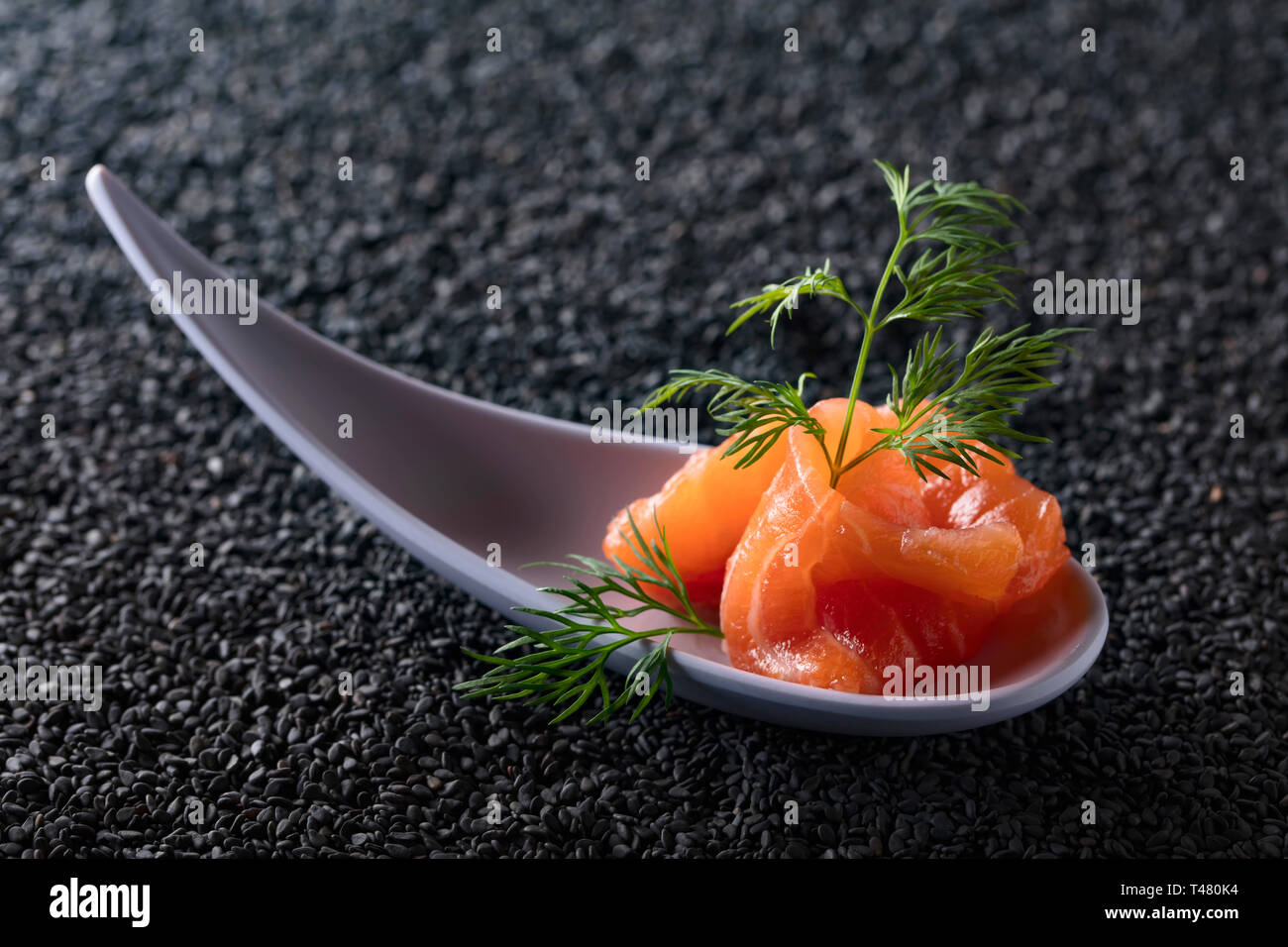 Slice of salted salmon with dill on the background of black sesame ...
