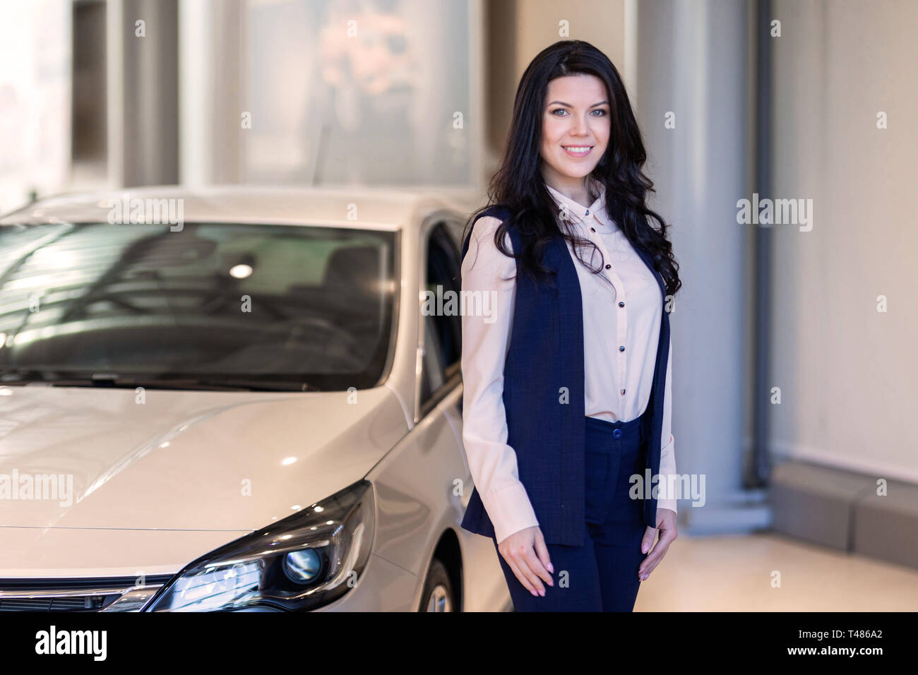 Beautiful woman in dealership center staying near new car. Shows ...