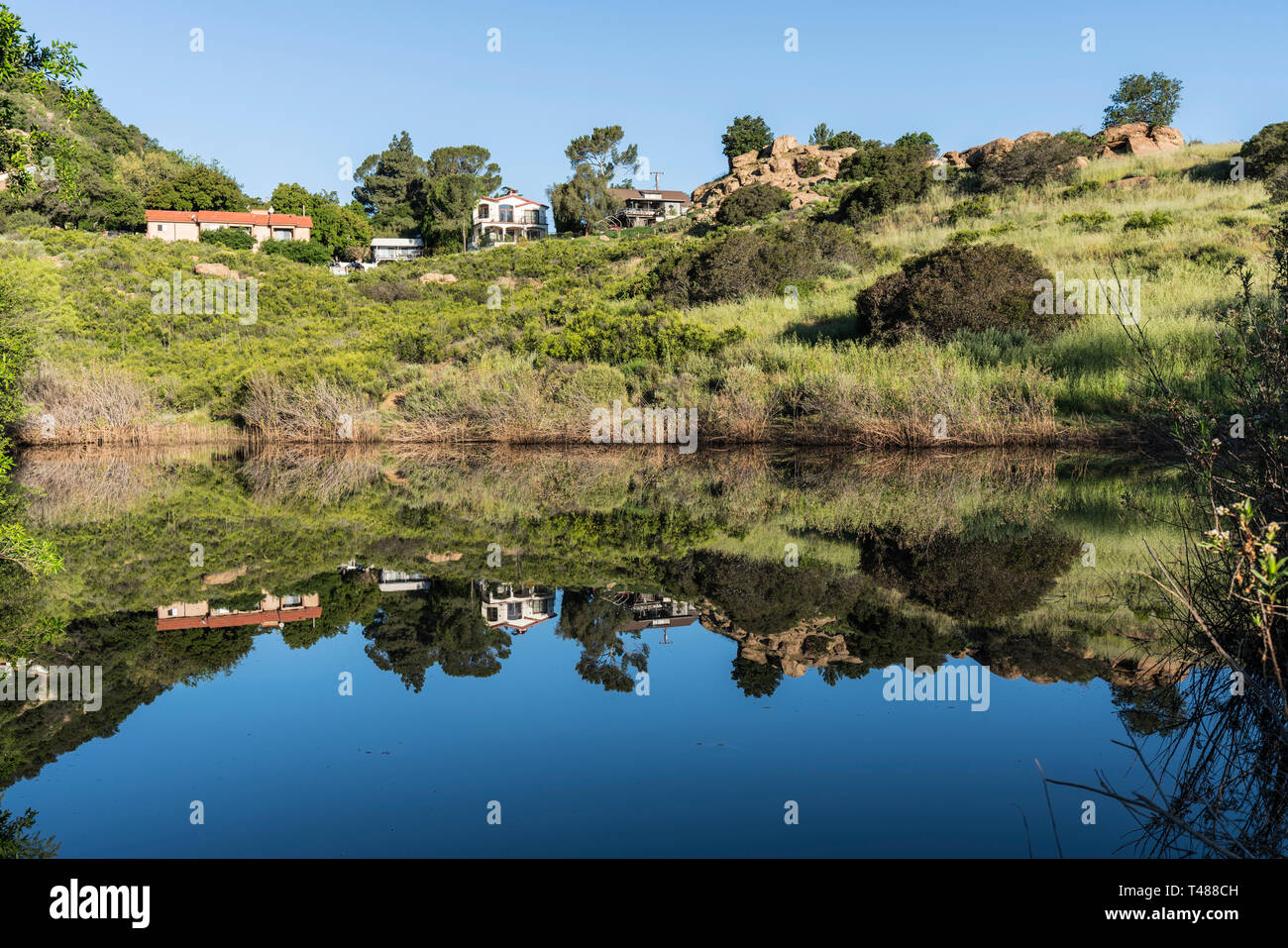 Canyon homes and rock formations reflecting in spring fed mountain pond ...