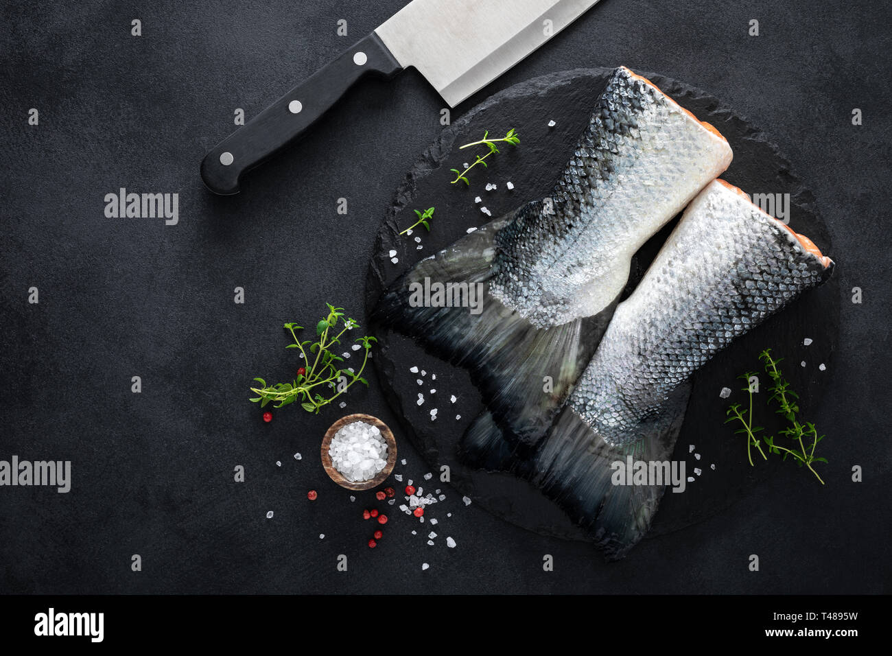 Raw salmon fishtails with ingredients for cooking on black background ...