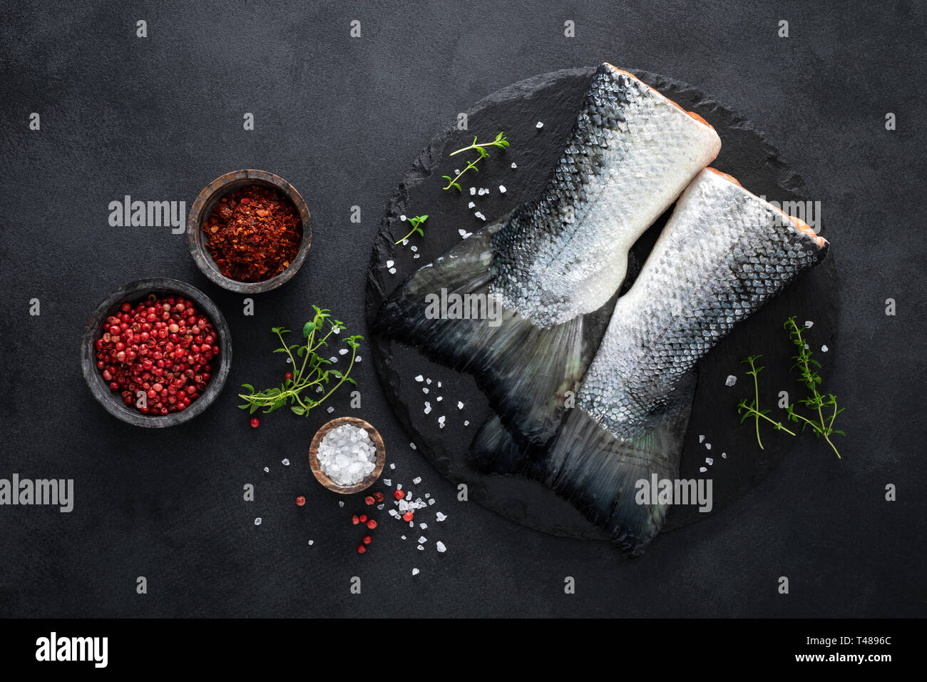 Raw salmon fishtails with ingredients for cooking on black background ...