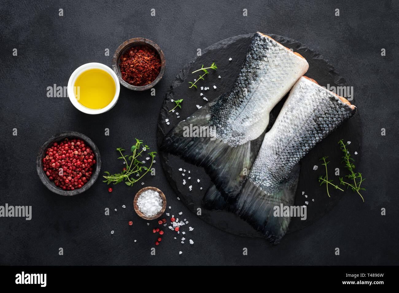 Raw salmon fishtails with ingredients for cooking on black background ...
