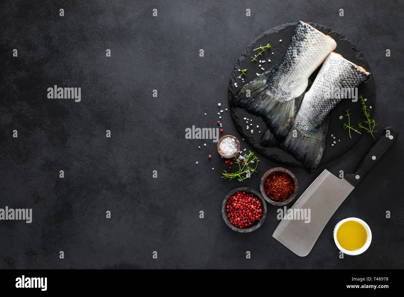 Raw salmon fishtails with ingredients for cooking on black background ...