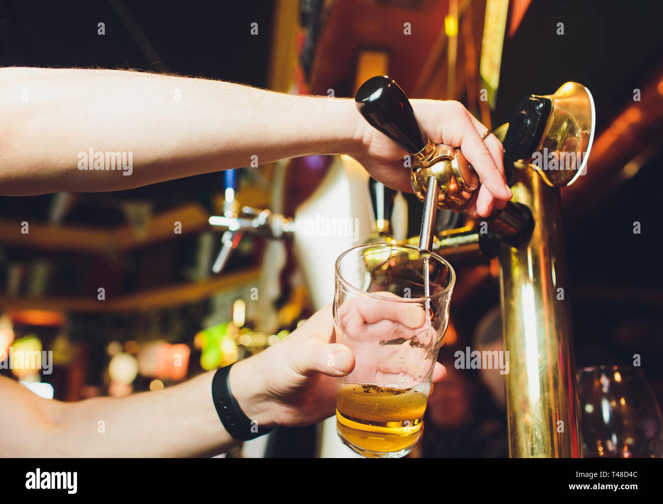 We meet oktoberfest. Hand of bartender pouring a large lager beer in tap. Pouring beer for ...