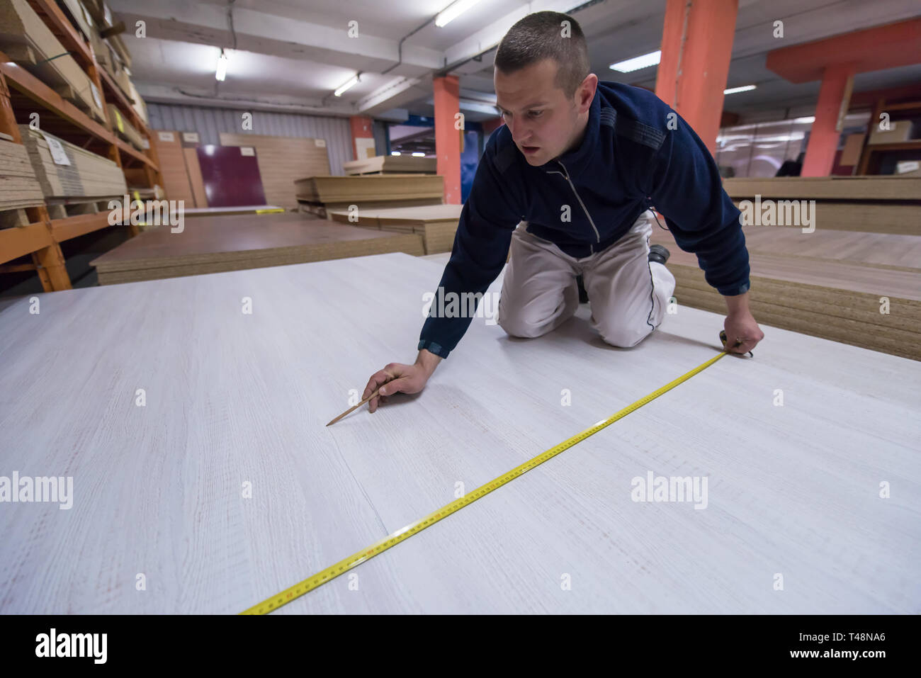 young man carpenter measuring wooden board for cutting while working in ...