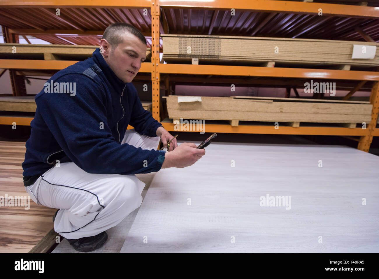 young man carpenter using a mobile phone to calculate measures for ...