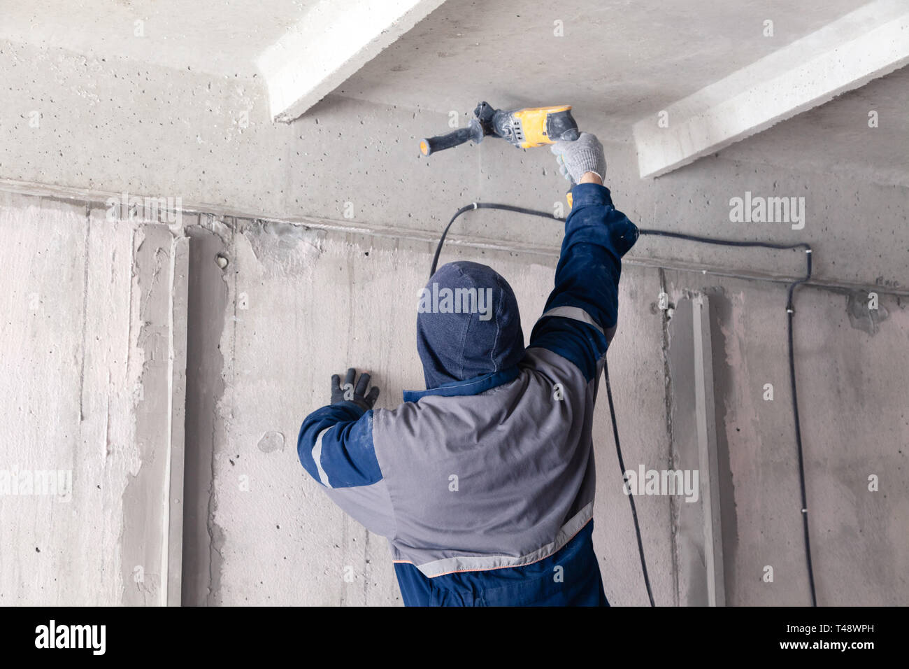 Worker builder makes electrical wiring, drills the ceiling with a drill ...