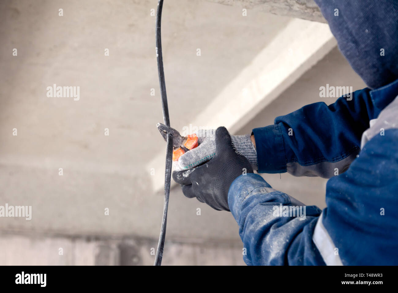 Worker builder makes electrical wiring, bites with tongs a black ...