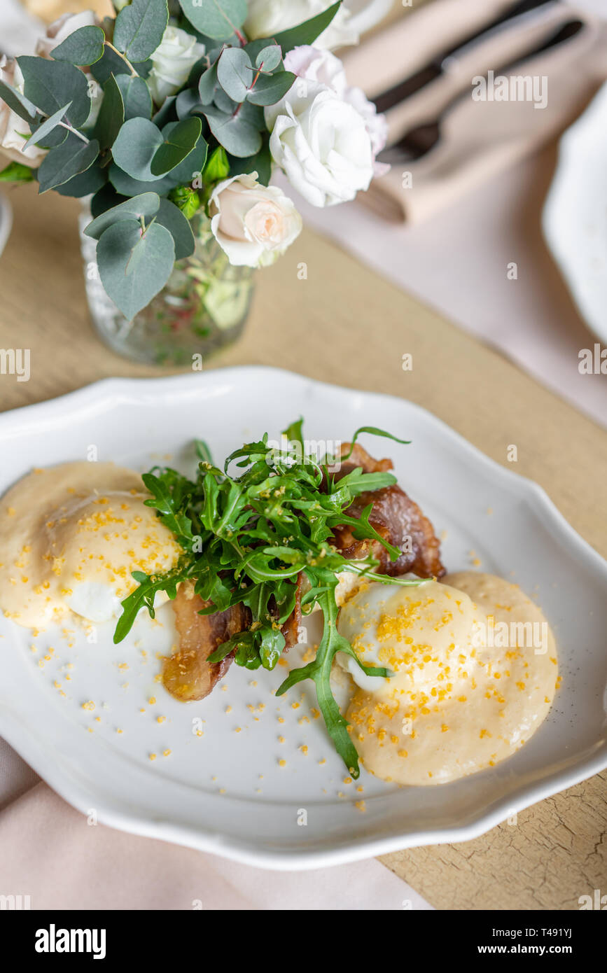 Egg Benedict with little salad on the plate with bacon and arugula. Two ...