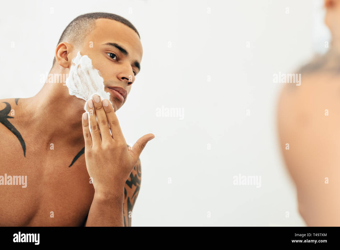 Handsome man applying shaving cream on his cheek in front of a mirror ...