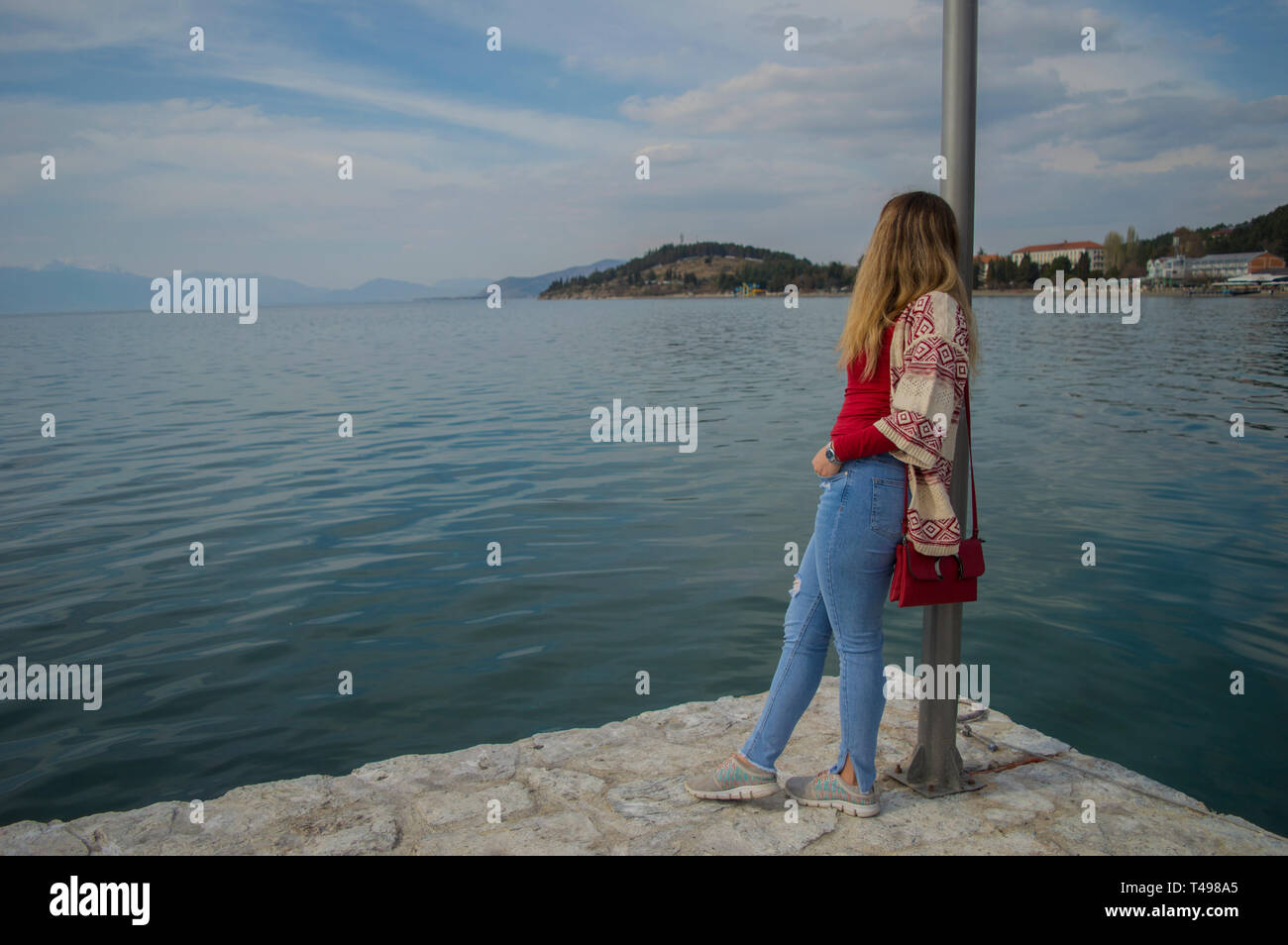 Girl leaning on a lamp post on a pier looking the lake and the ...