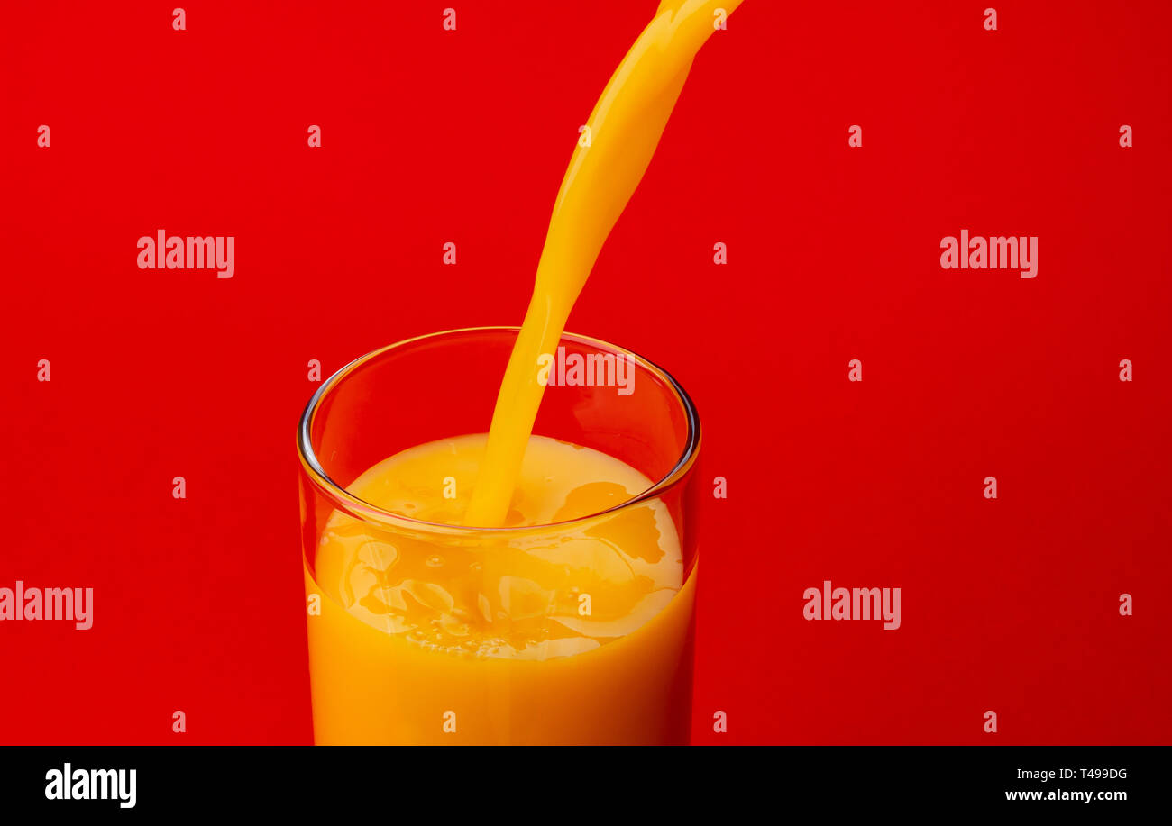 Orange juice pouring into glass, isolated on red color background, with ...