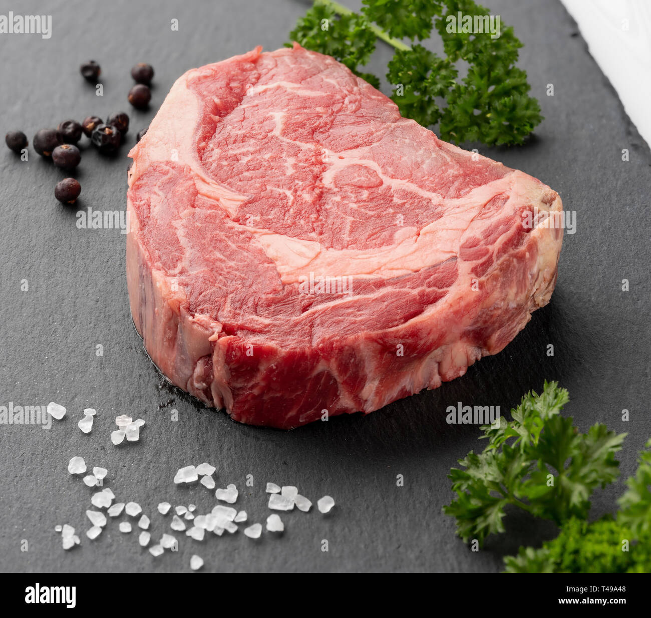 Raw ribeye steak on a slate with juniper berries and parsley Stock ...