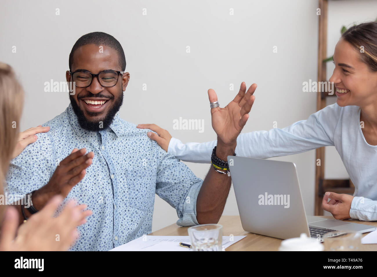 Friendly caucasian team employees tap african colleague on shoulder ...