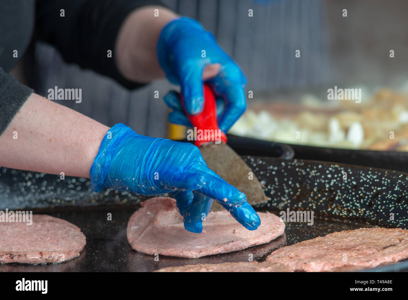 Cooking burgers on a griddle wearing blue gloves to meet food hygiene ...
