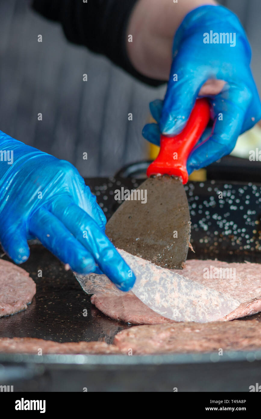 Cooking burgers on a griddle wearing blue gloves to meet food hygiene ...