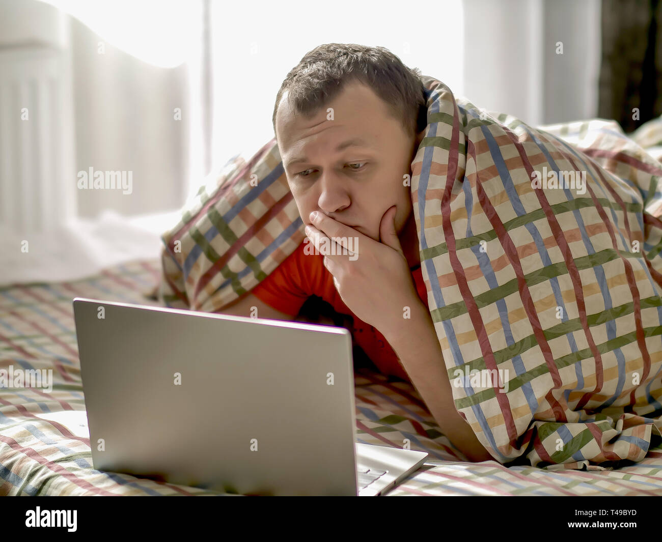guy lying on the bed under the covers and looking into the laptop Stock ...
