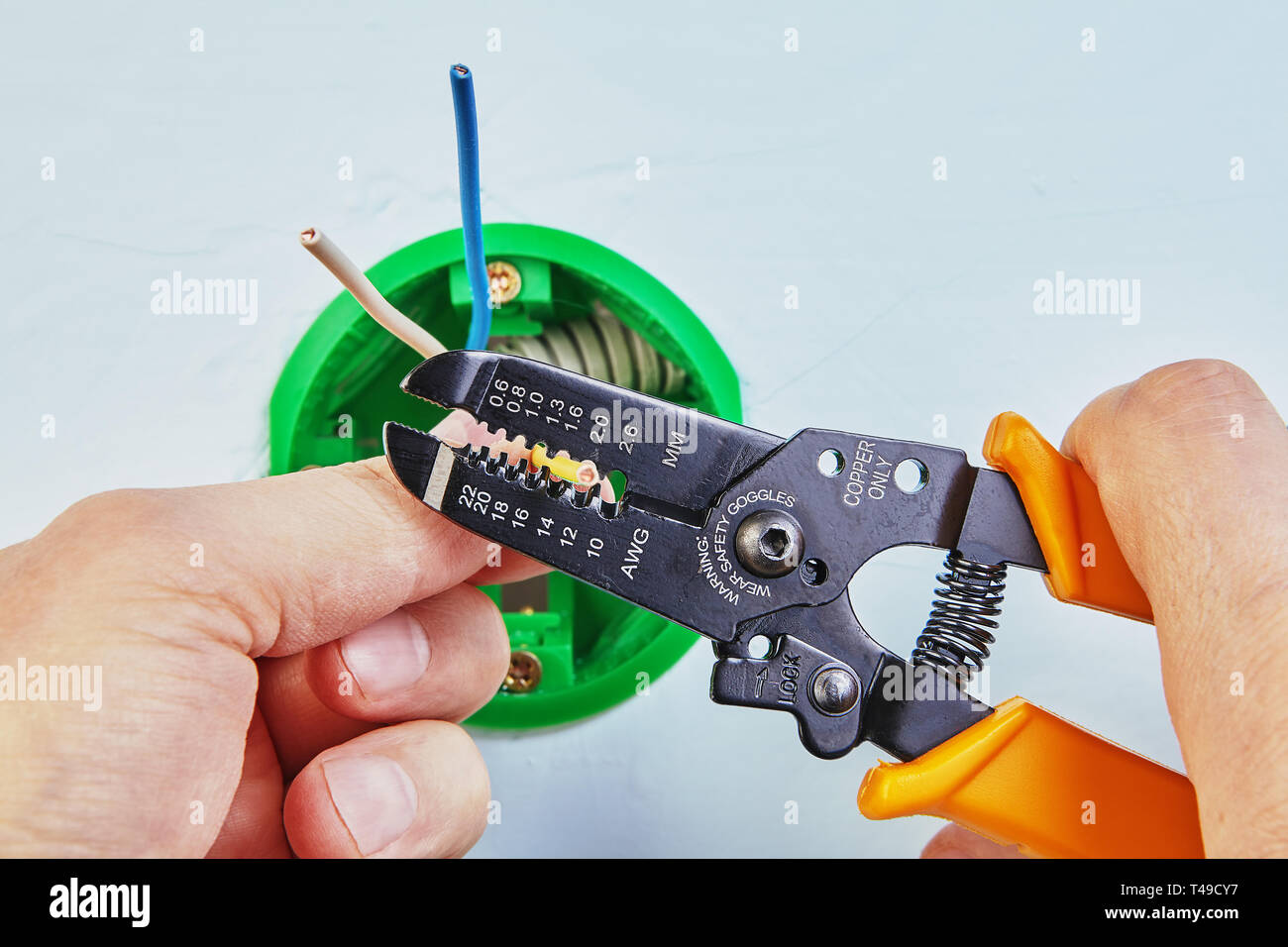 Electrician is removing insulation from wires of round electrical box with wire stripper cutter Stock Photo Alamy