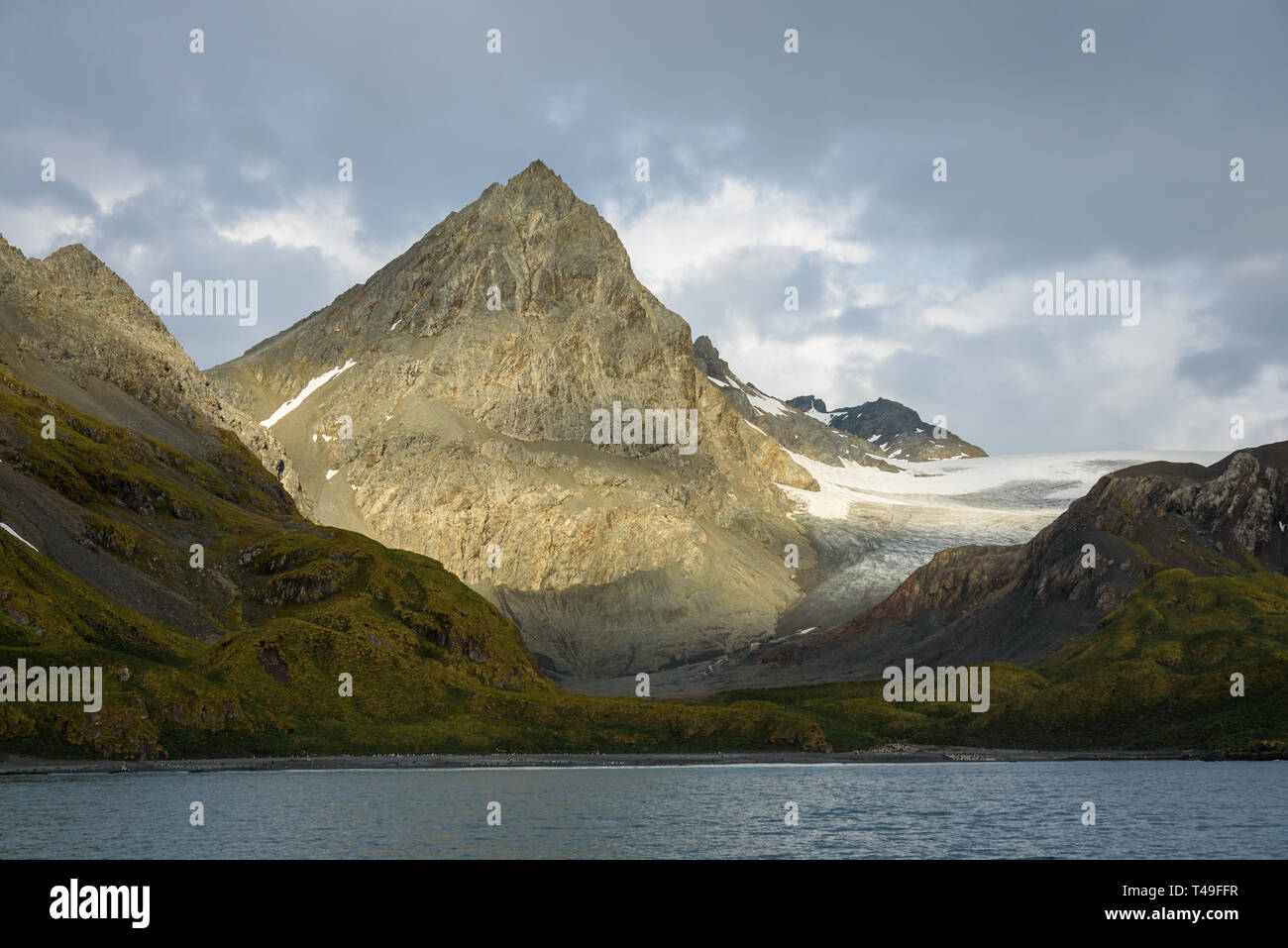Sharp mountain peak highlighted by the sun against a stormy sky ...