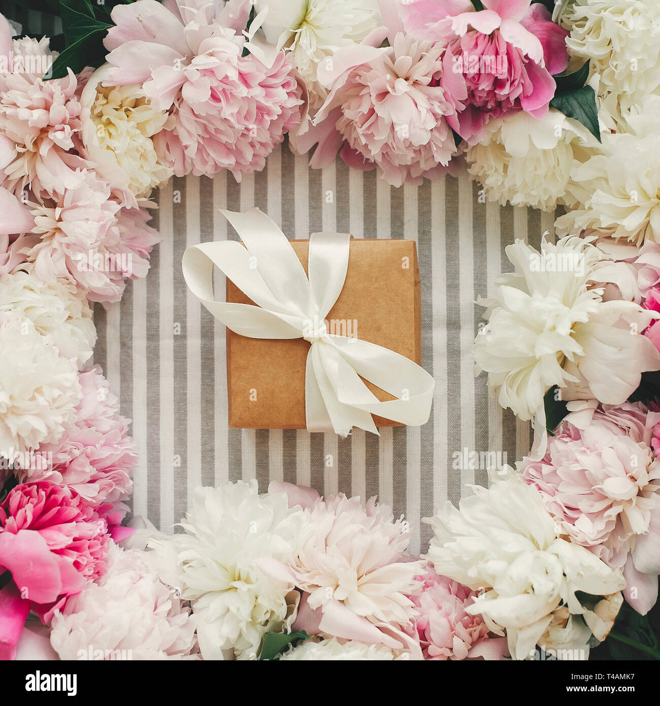 Beautiful gift box with ribbon in pink and white peonies frame on table ...