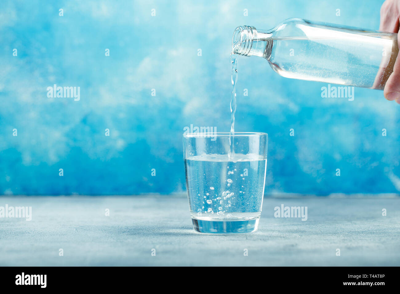 Pouring clear water from bottle into glass on blue background Stock ...