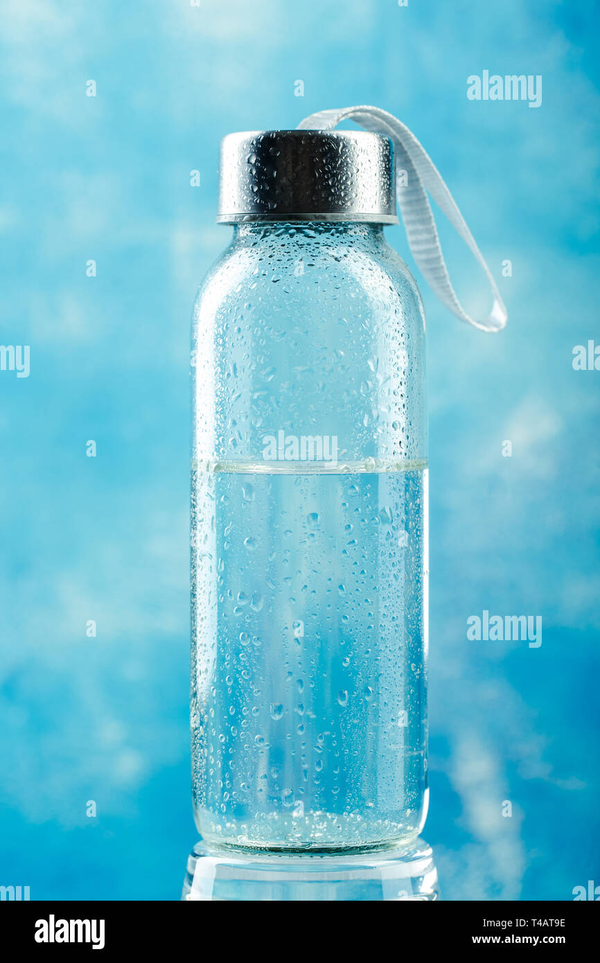 Small glass water bottle with drops on blue background Stock Photo - Alamy