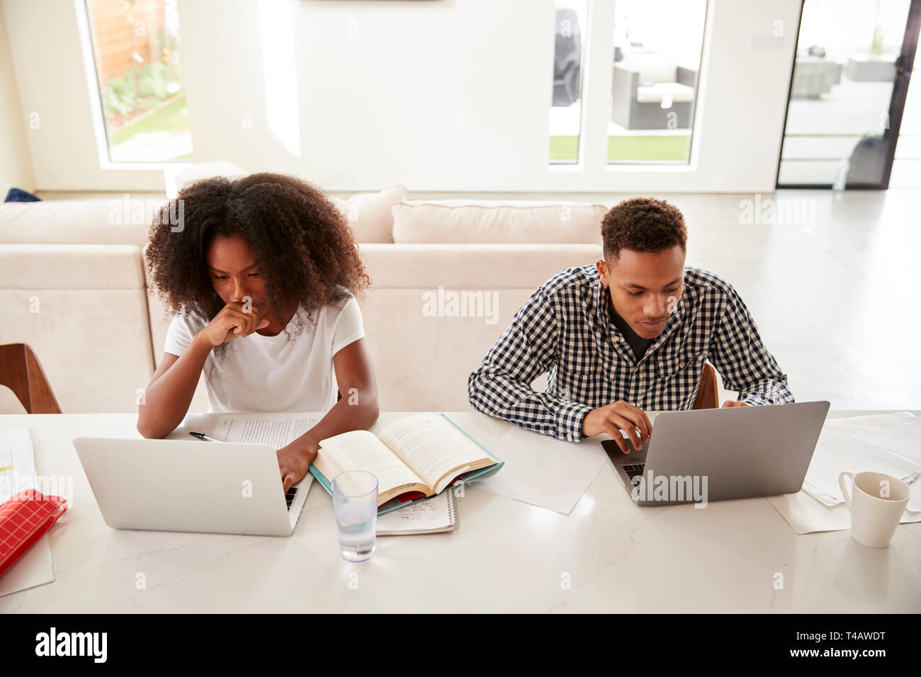 Black teenage brother and sister sitting at home using laptop computers ...