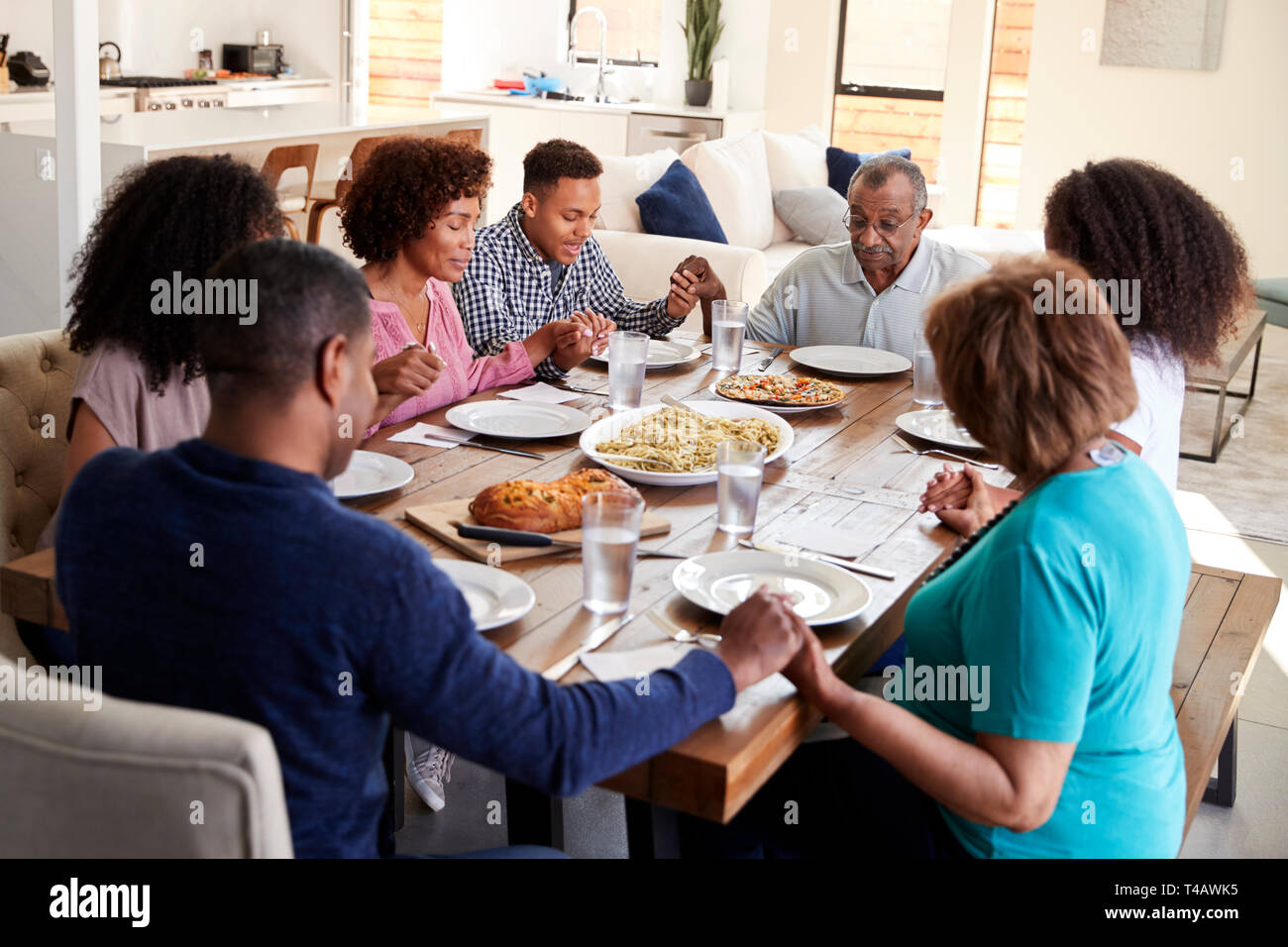 Three generation black family sitting at dinner table holding hands and ...