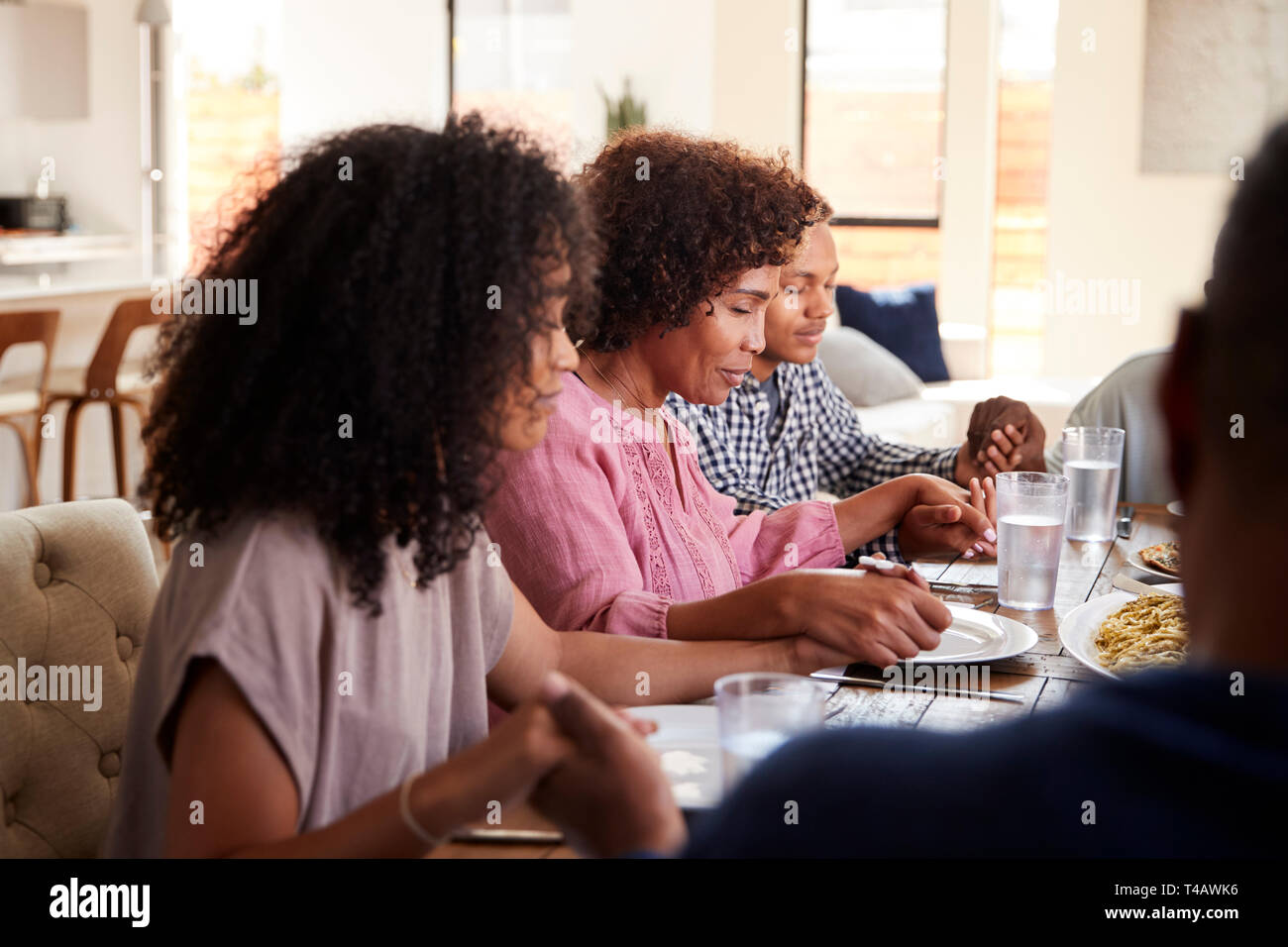 Close up of black family sitting at dinner table holding hands and ...