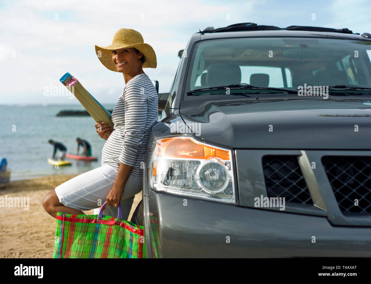 Woman leaning against car holding beach gear Stock Photo - Alamy