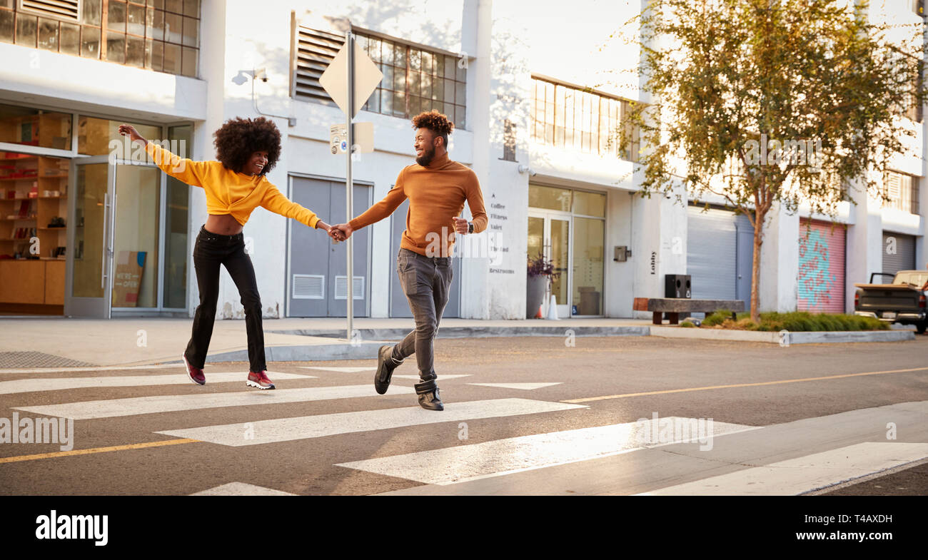 Fashionable young black couple running across a city street holding ...