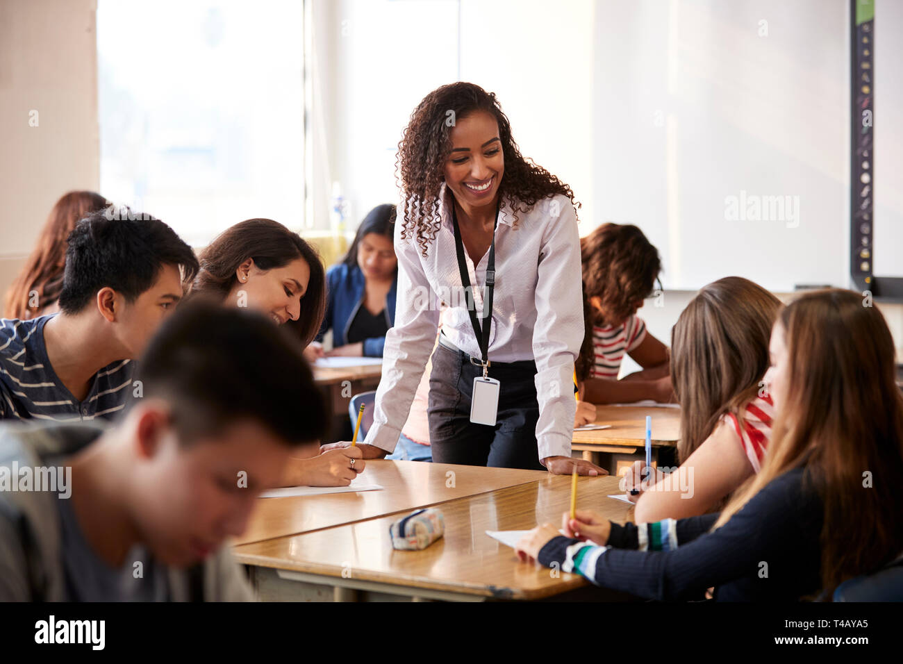 Female High School Teacher Standing By Student Table Teaching Lesson ...