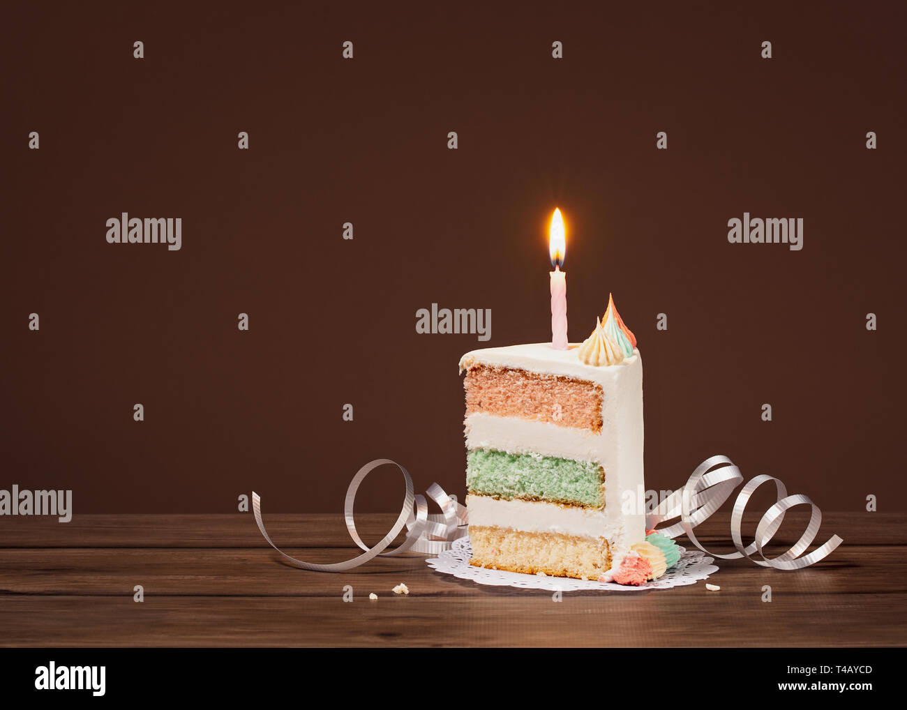 Birthday cake slice with three pastel colored layers and lit candle on ...