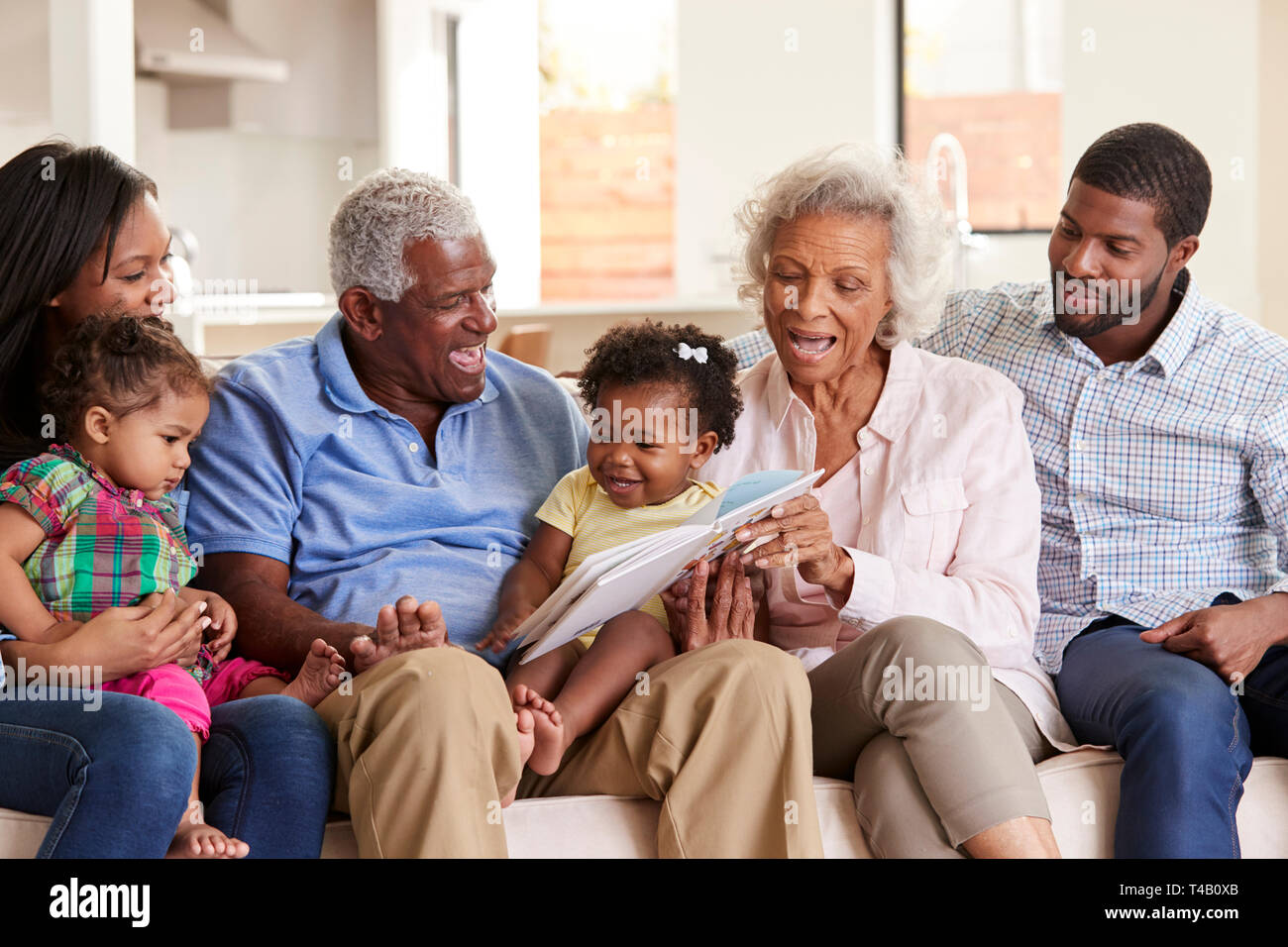 Multi-Generation Family Sitting On Sofa At Home Reading Book With Baby ...