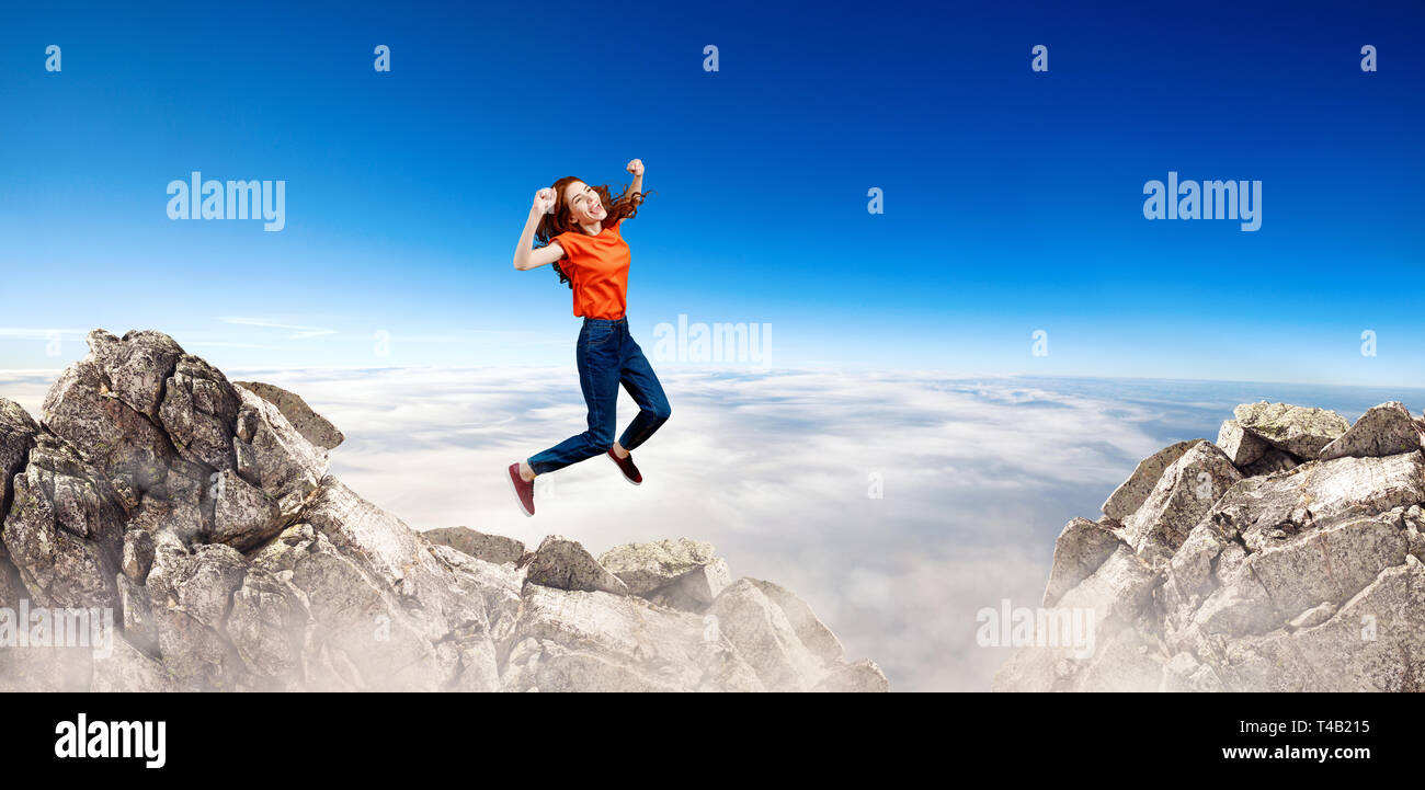 Redhead woman jumps over cliff on blue sky background Stock Photo - Alamy